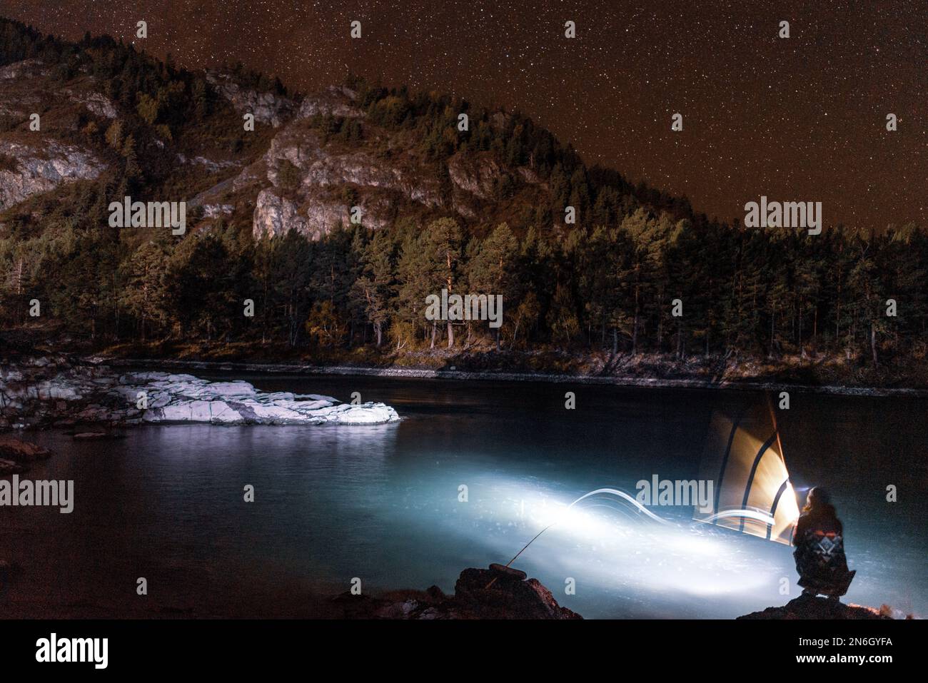 The silhouette of a fisherwoman girl with a lantern waves a fishing rod ...