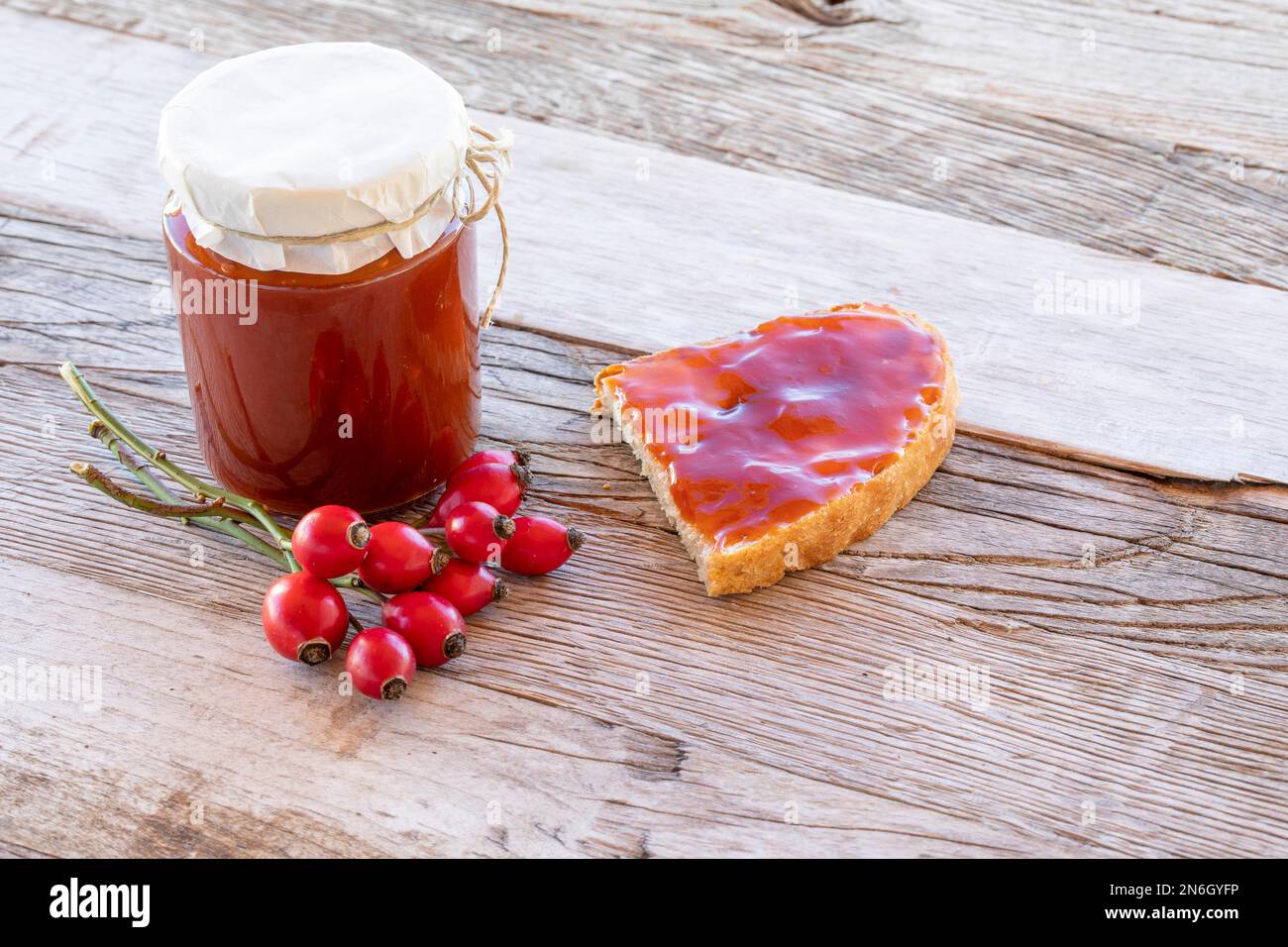Homemade rosehip jam in a jar and slice of bread with spread on wooden ...