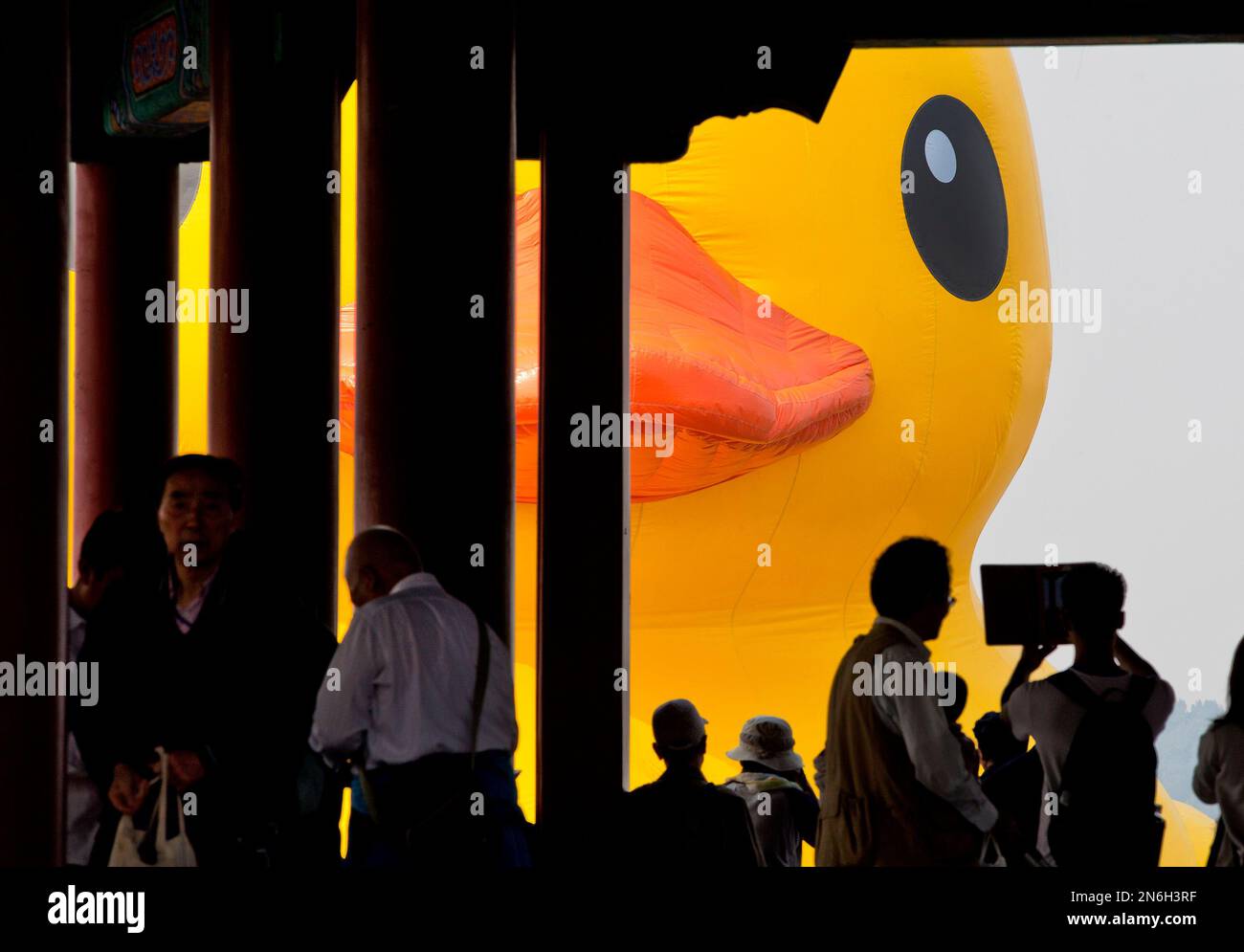 Visitors in a traditional pavilion take photos of a giant yellow rubber ...