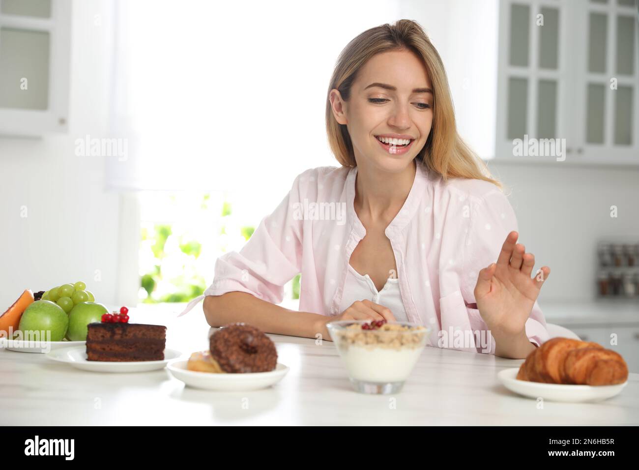 Woman choosing between sweets and healthy food at white table in ...