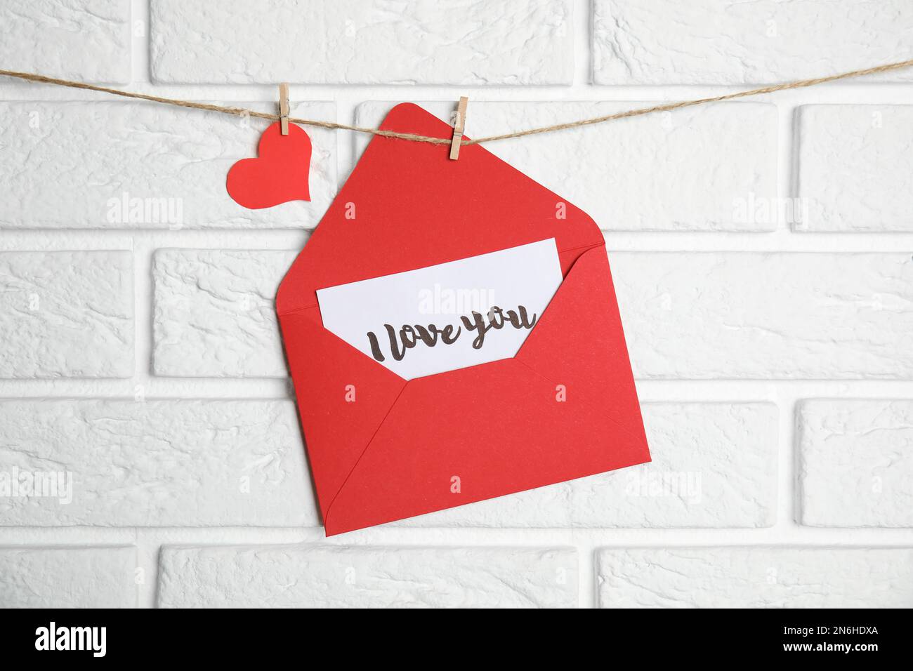 Envelope with I Love You card hanging on twine near white brick wall ...