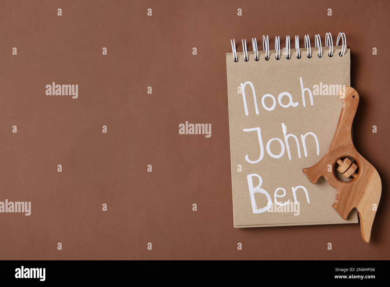 Notebook with list of baby names and wooden toy on brown background ...