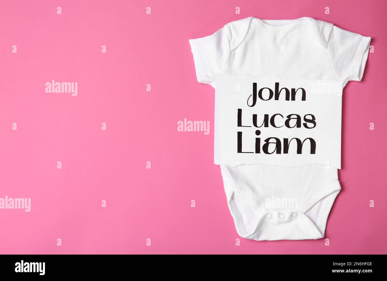 Bodysuit with different baby names on pink background, top view. Space ...
