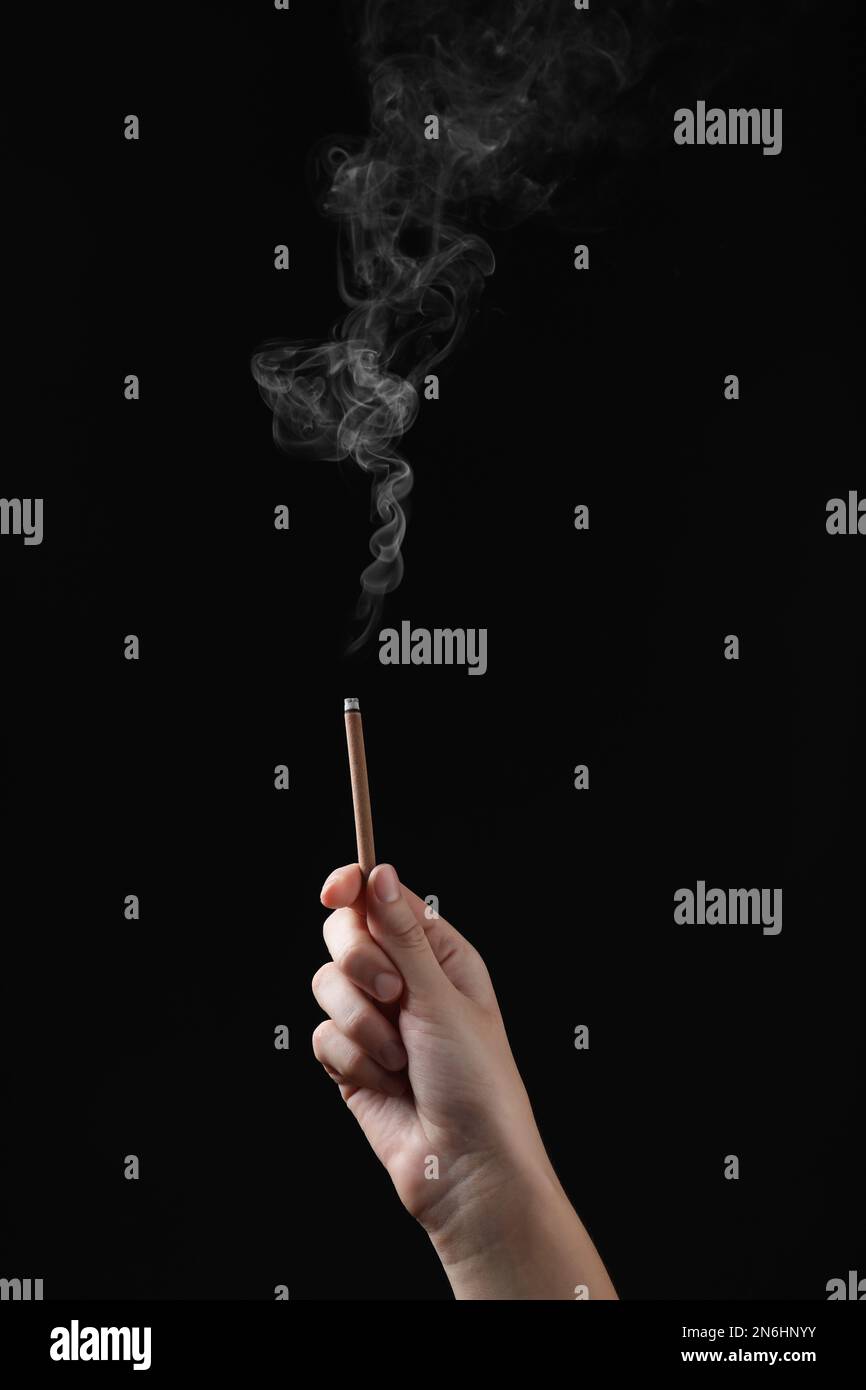 Woman holding smoldering incense stick on black background, closeup ...
