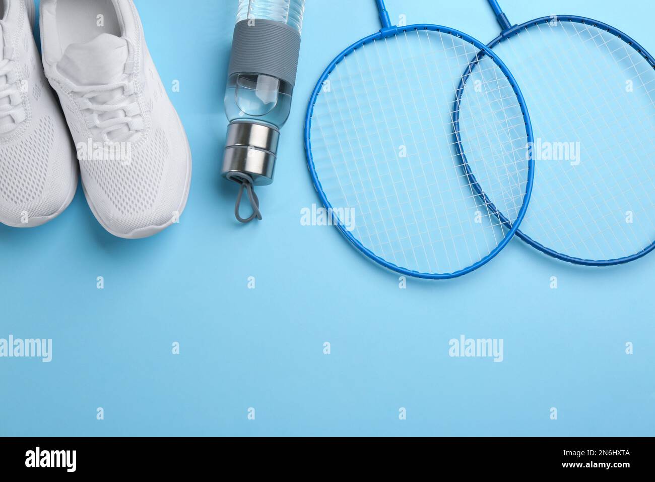 Badminton rackets, bottle and shoes on light blue background, flat lay ...