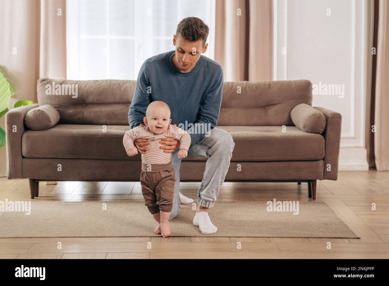 Baby boy taking his first steps with father's help at home. Happy young ...