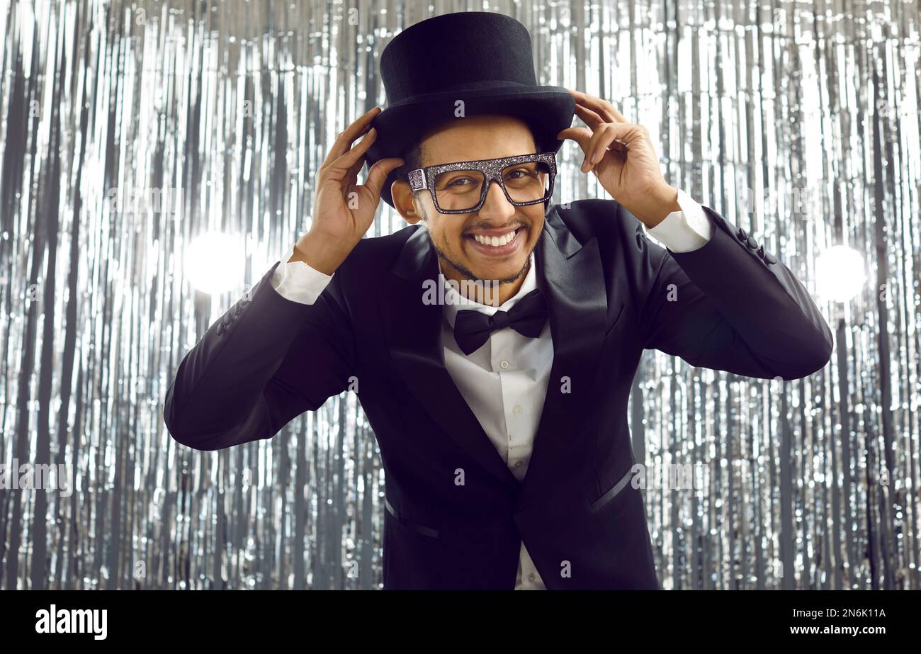 Funny young black man in a dinner suit, top hat and glasses having fun ...