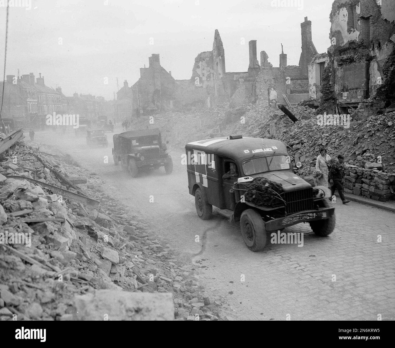 Heavy traffic on the move through the wrecked streets of Isigny, France ...