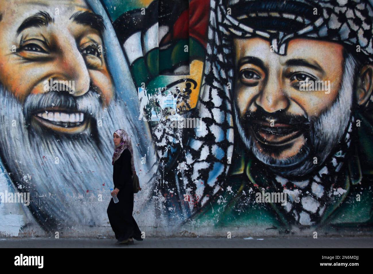 A Palestinian student walks in front of a mural depicting the late ...