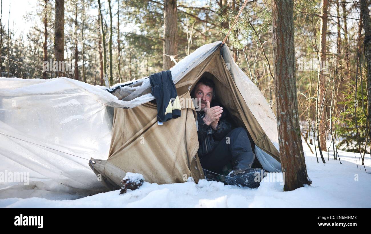 A homeless man climbs in and out of a tent in the woods in winter Stock ...