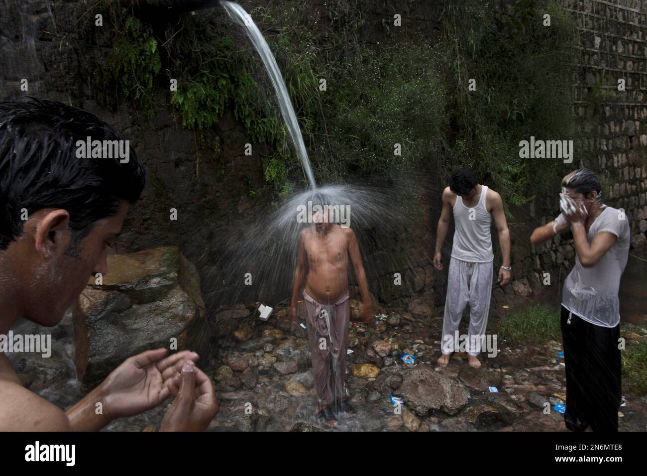 Pakistani daily laborers take a shower under a leaking water supply ...