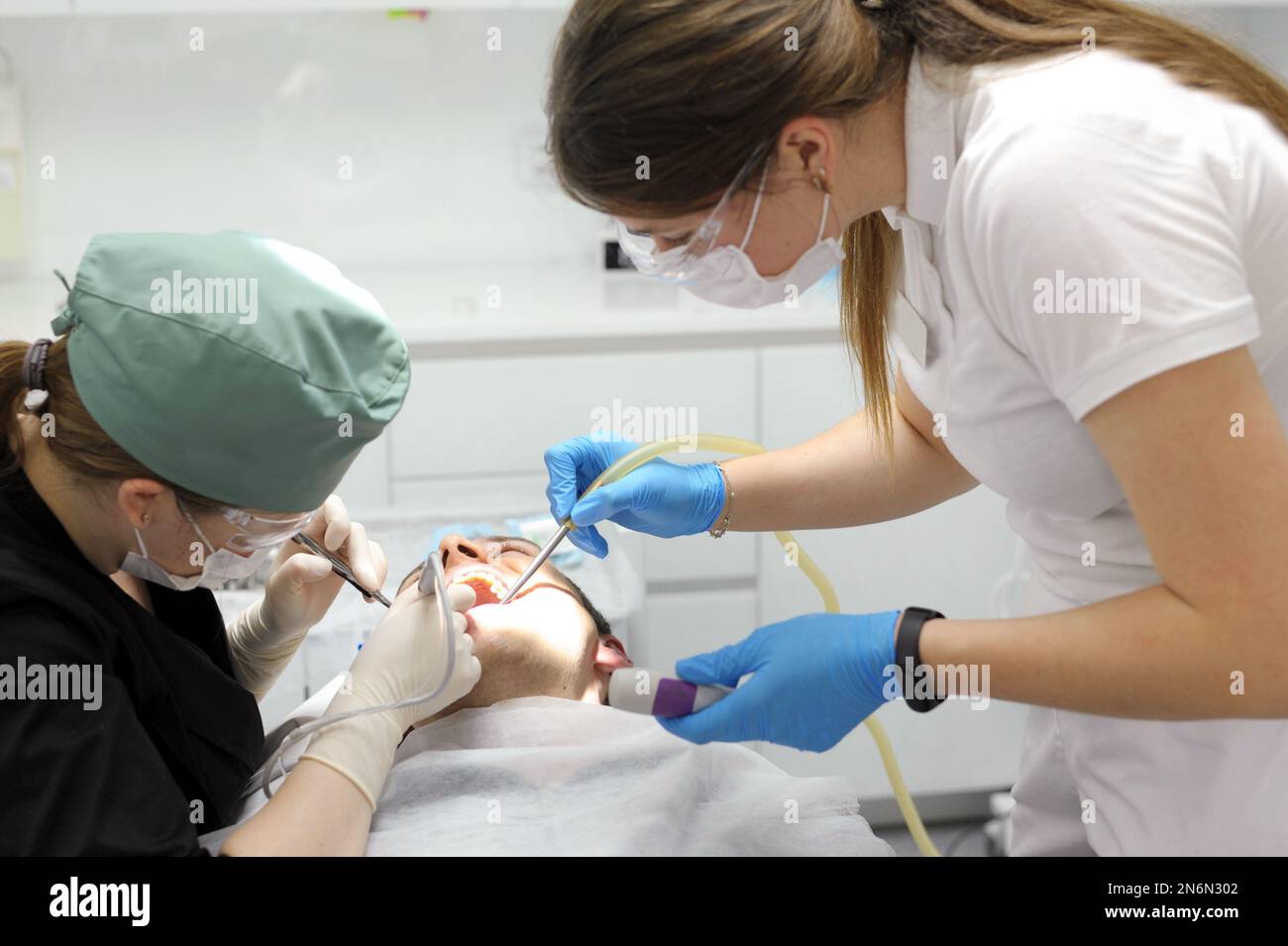 dentistry doctor treats a tooth in man patient women in masks on them ...