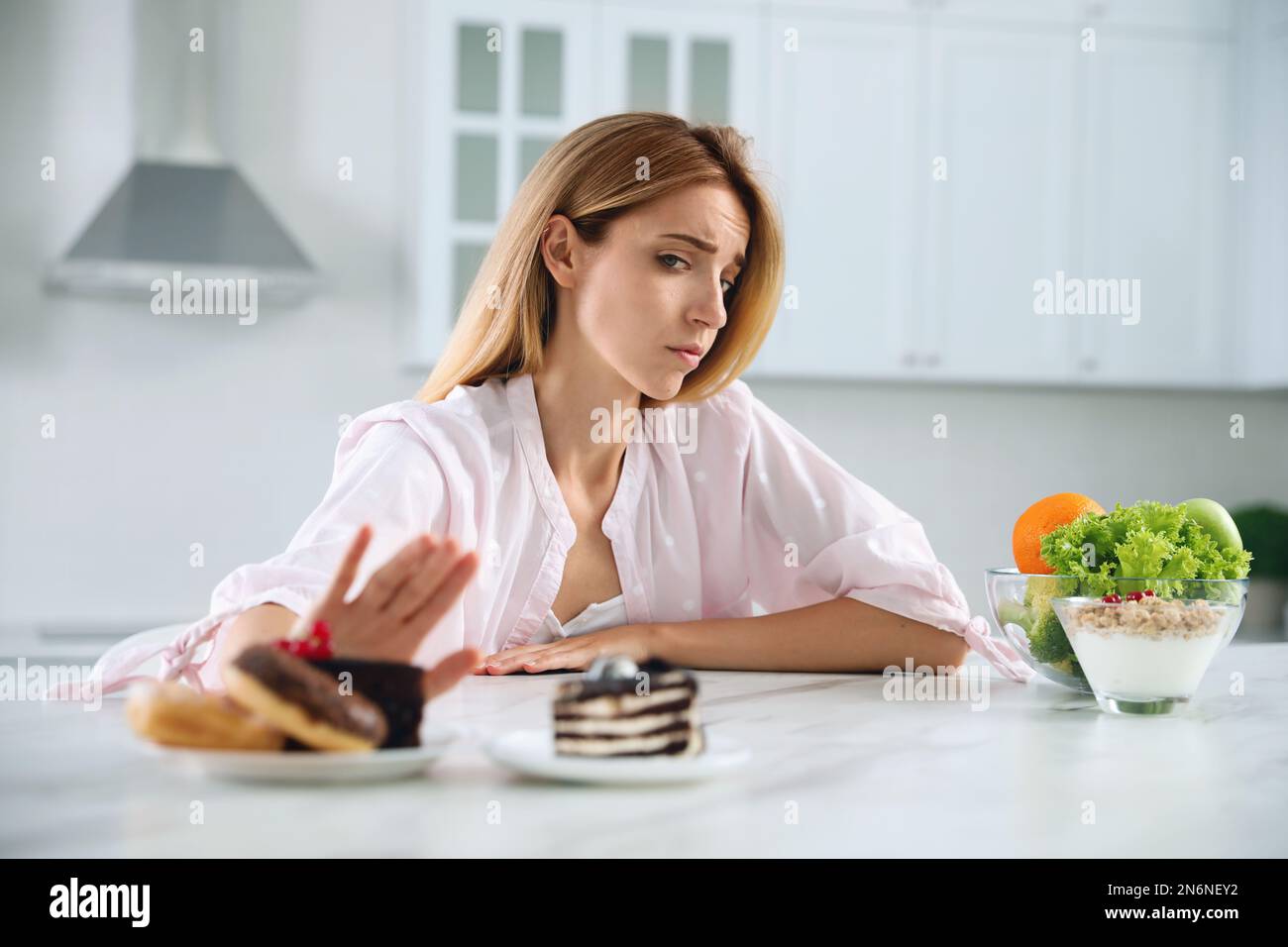 Woman choosing between sweets and healthy food at white table in ...