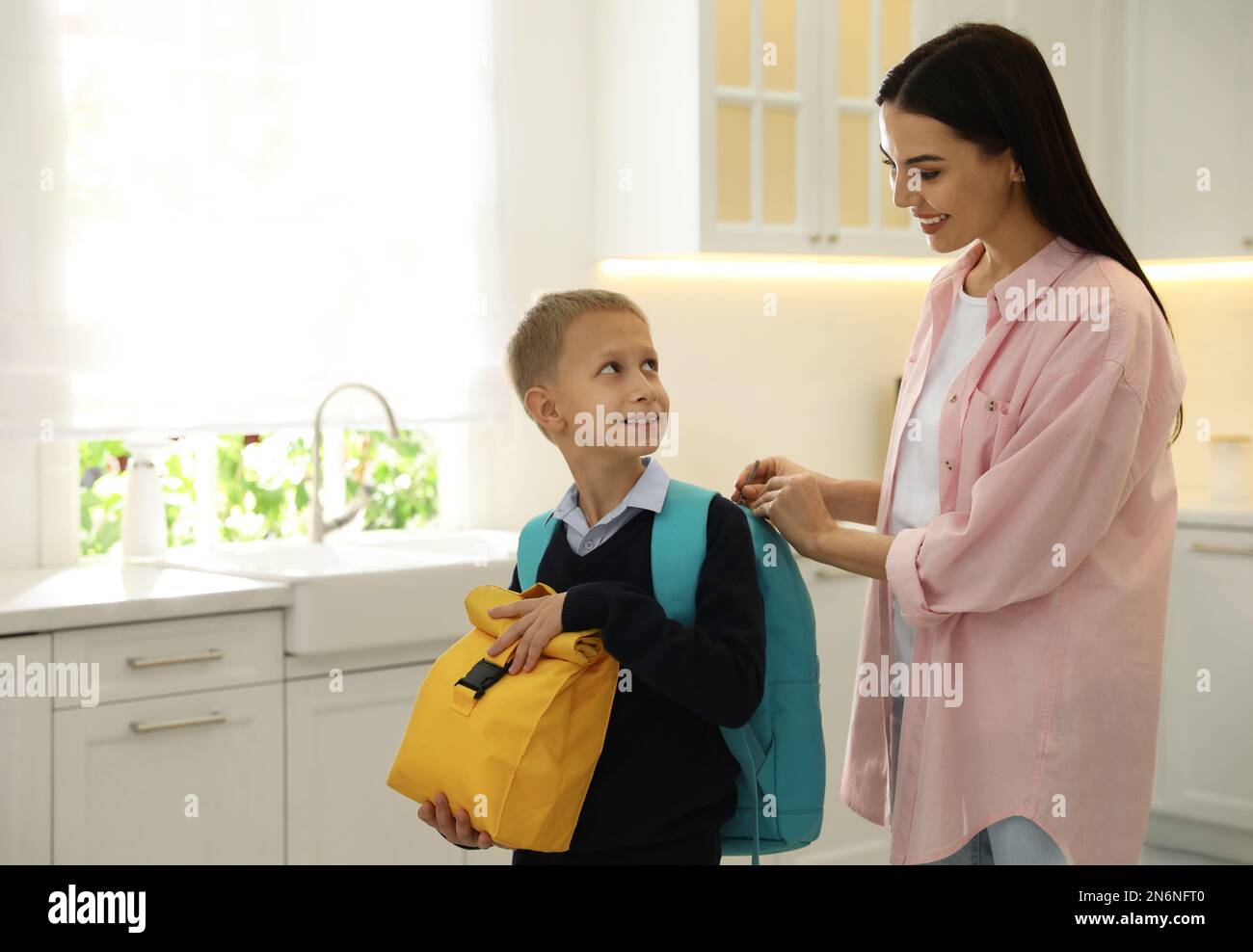 Young mother helping her little child get ready for school in kitchen ...