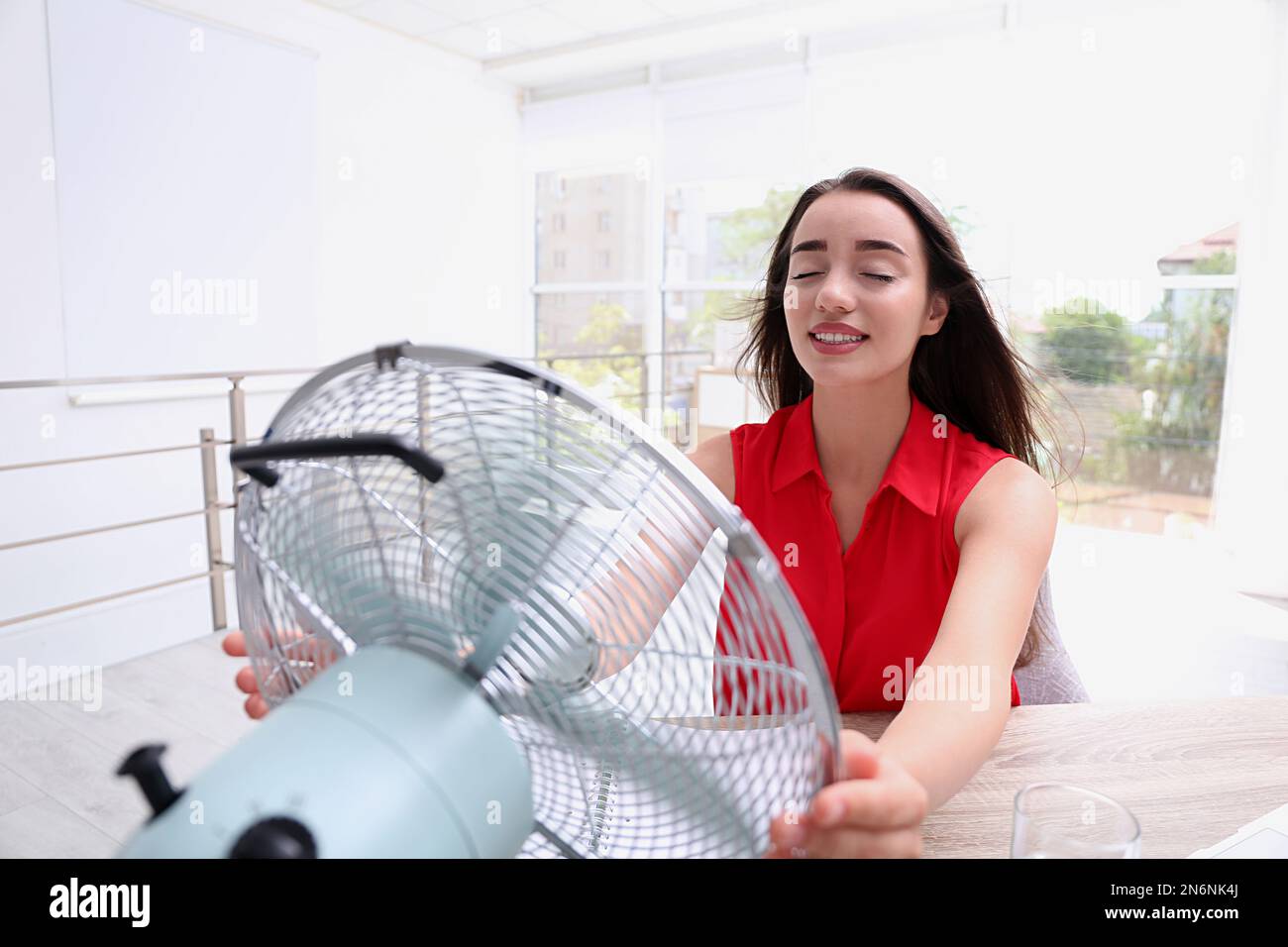 Young woman enjoying air flow from fan at workplace. Summer heat Stock ...