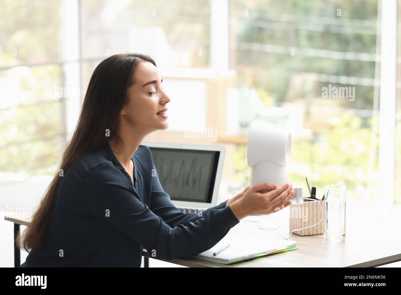 Young woman enjoying air flow from portable fan at workplace. Summer ...