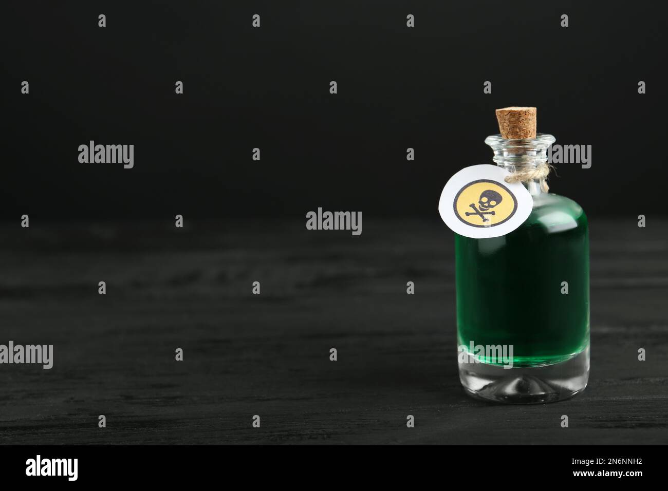 Glass bottle of poison with warning sign on black wooden table. Space ...