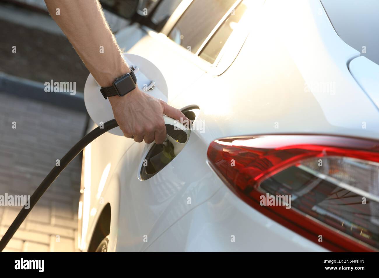 Man inserting plug into electric car socket at charging station ...