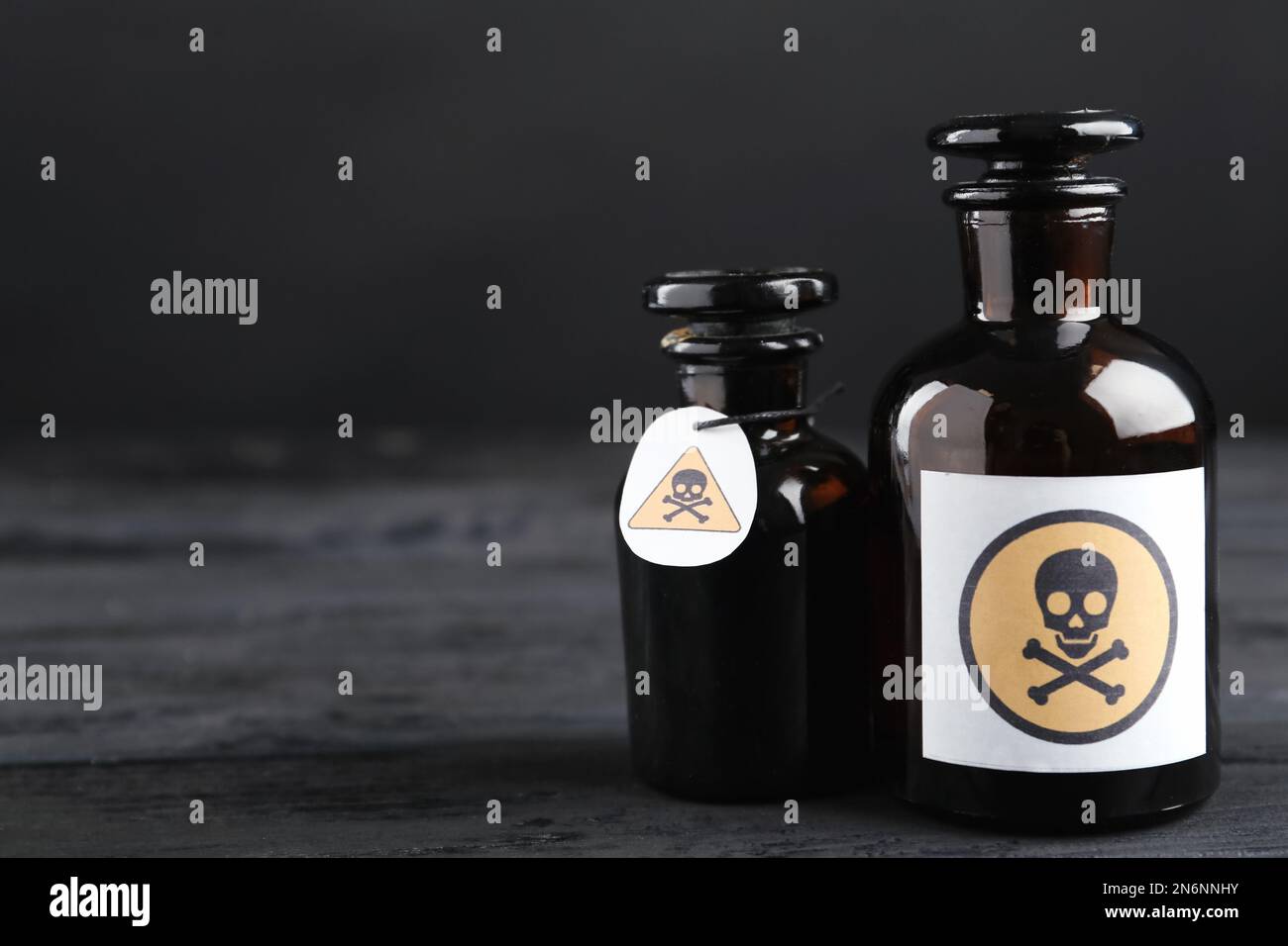 Glass bottles of poison with warning signs on black wooden table. Space ...
