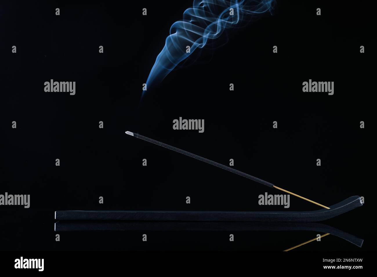 Incense stick smoldering in holder on black background Stock Photo - Alamy