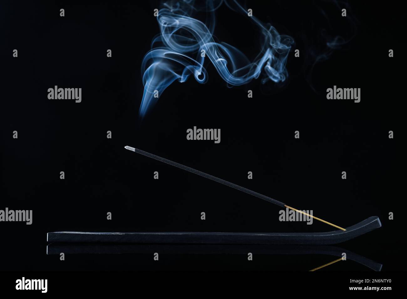 Incense stick smoldering in holder on black background Stock Photo - Alamy