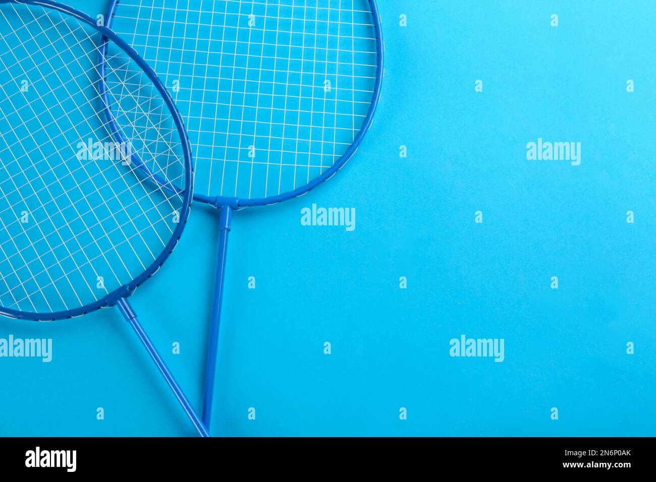 Badminton rackets on light blue background, flat lay. Space for text ...