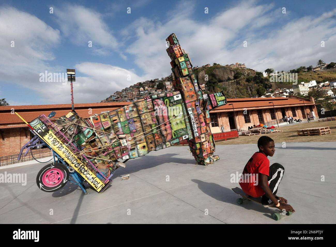 A youth rides his skateboard in a plaza where a sculpture stands on ...