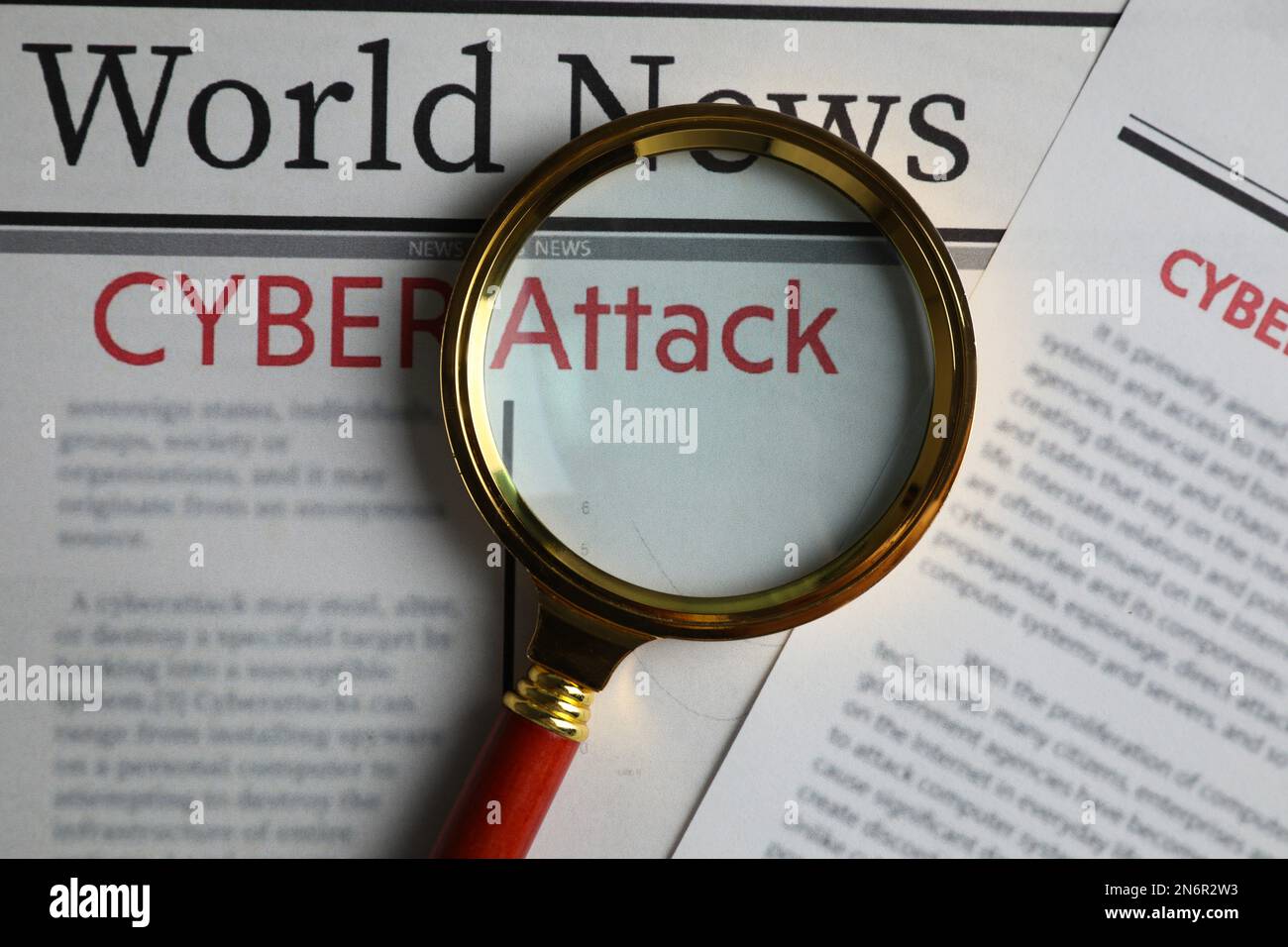 Newspaper with headline CYBER ATTACK and magnifying glass, top view ...