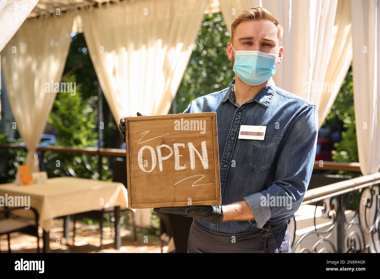 Waiter holding OPEN sign in restaurant. Catering during coronavirus ...