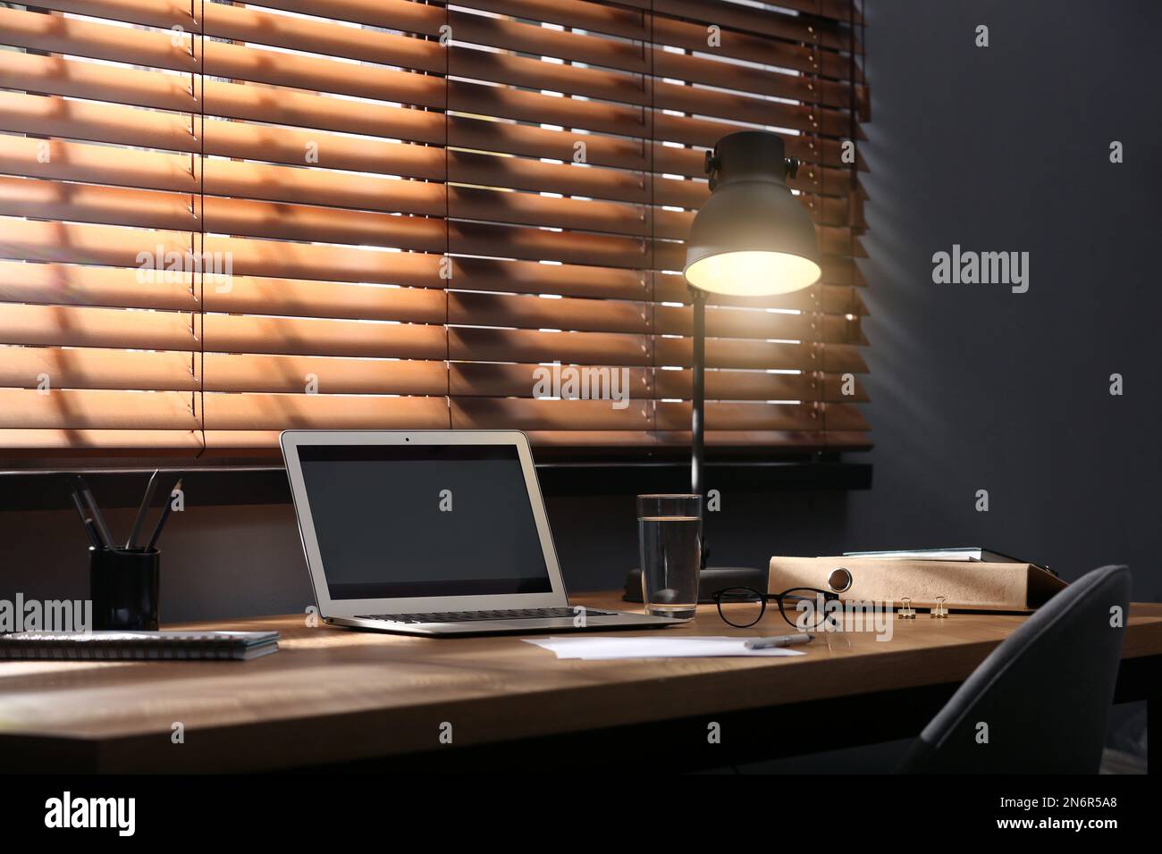 Modern laptop and lamp on table near window in office Stock Photo - Alamy
