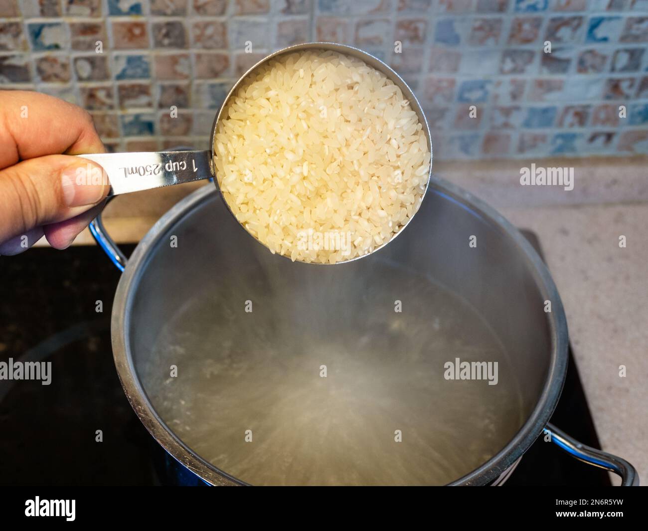 pouring rice groats from measuring cup into boiling water in saucepan ...