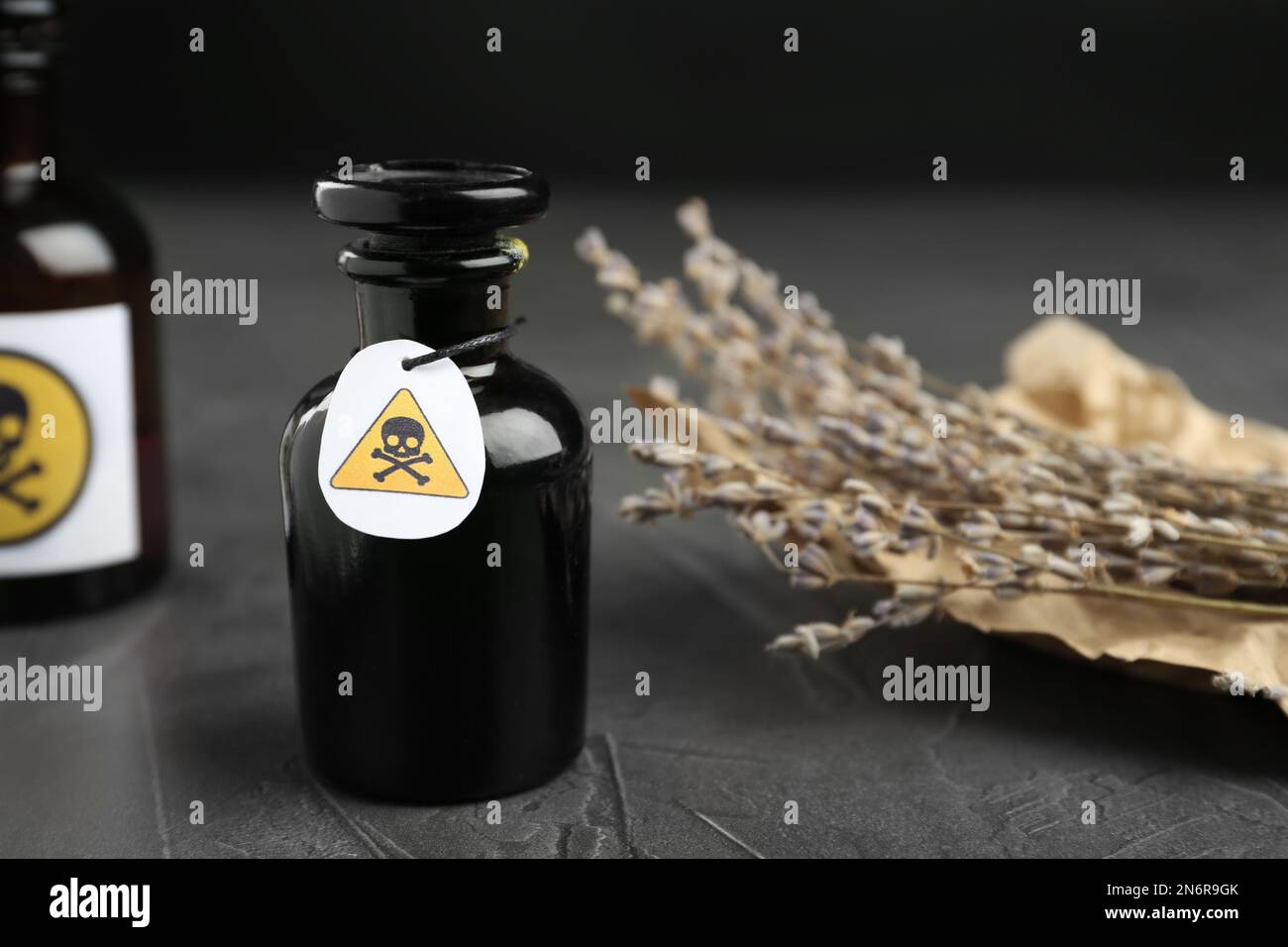Glass bottle of poison with warning sign and herb on grey stone table ...
