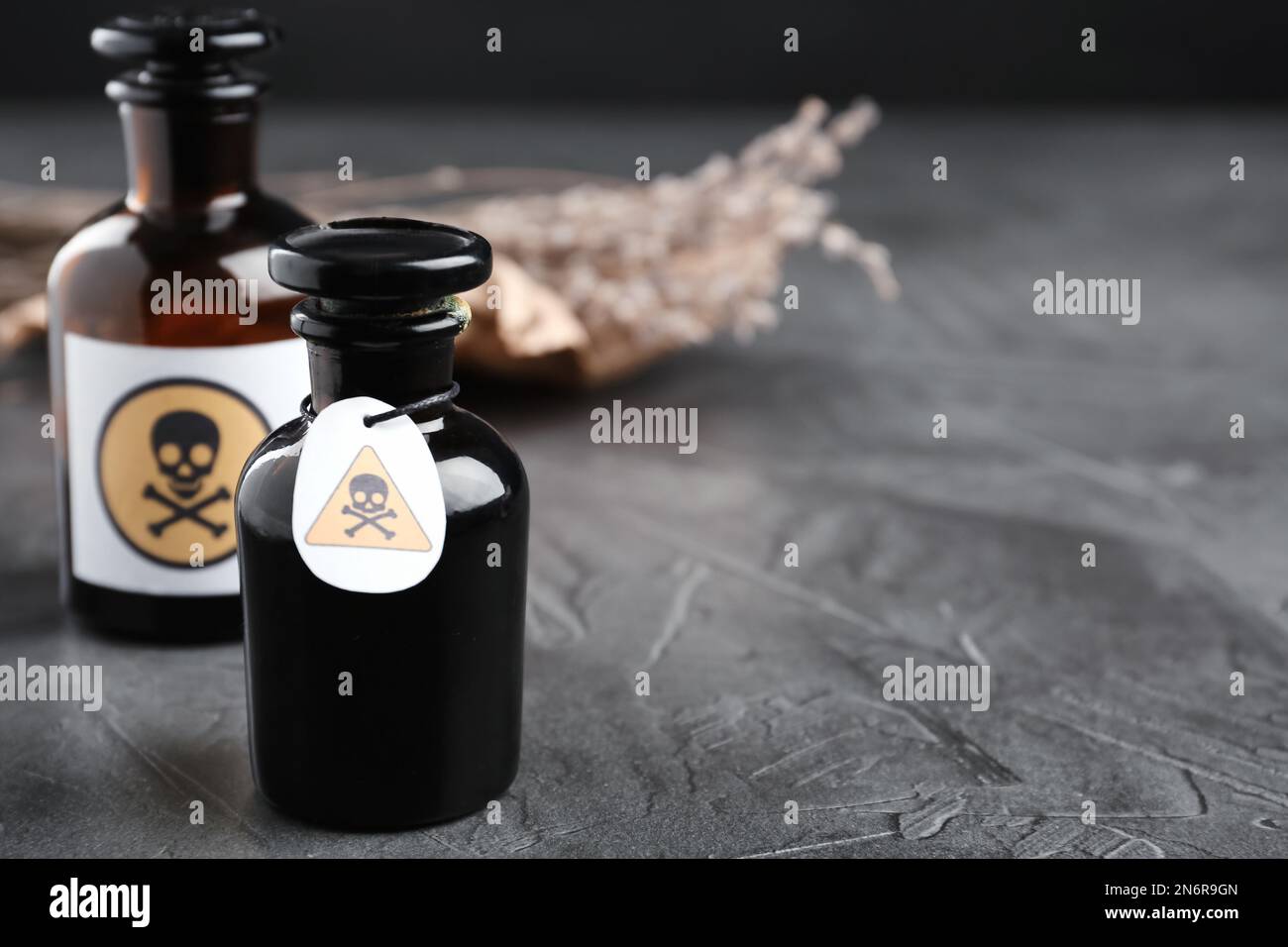 Glass bottles of poison with warning signs on grey stone table. Space ...
