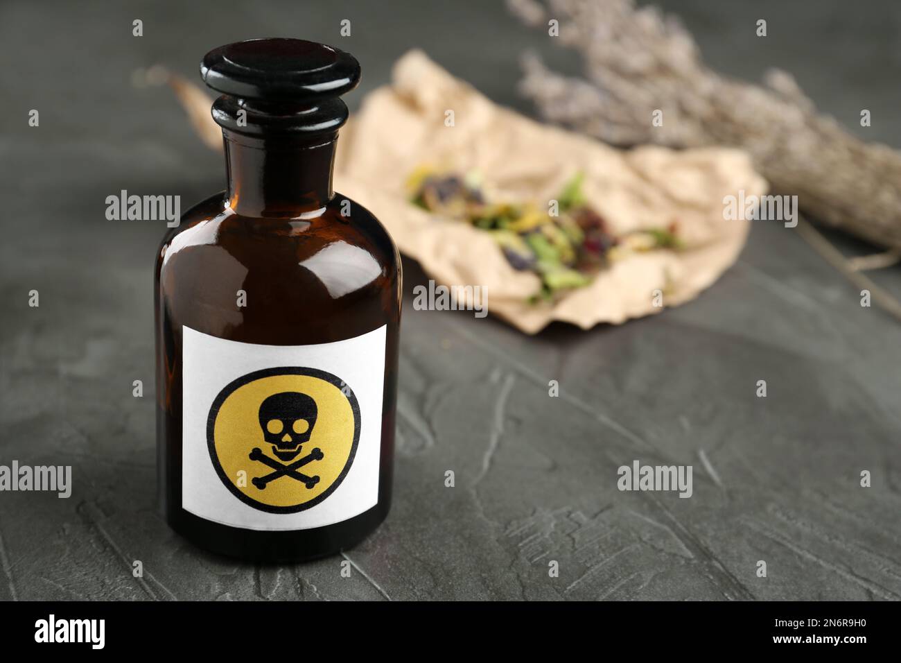 Glass bottle of poison with warning sign on grey stone table. Space for ...