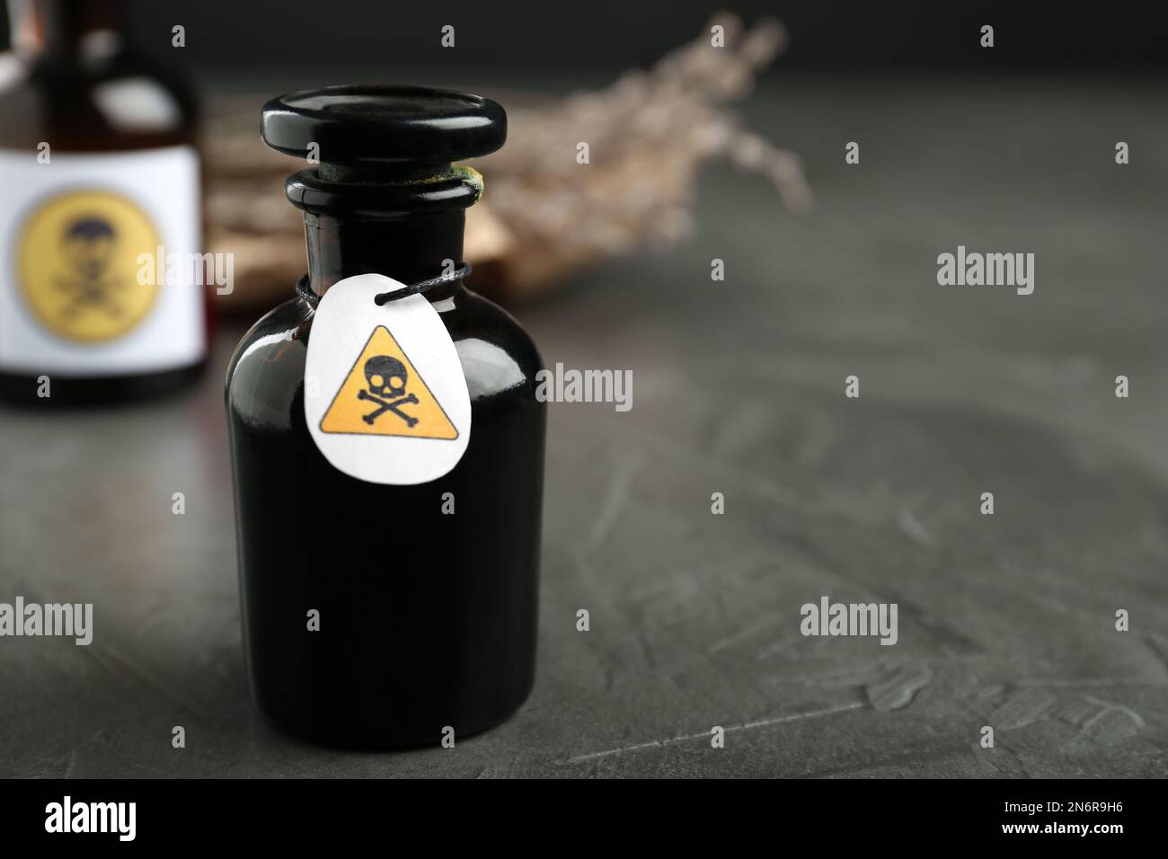 Glass bottle of poison with warning sign on grey stone table. Space for ...