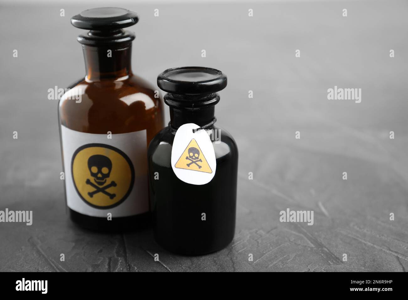Glass bottles of poison with warning signs on grey stone table. Space ...