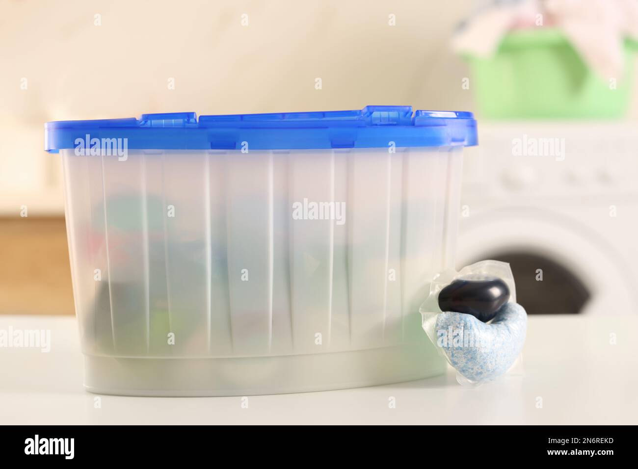 Laundry container and washing detergent capsule on table indoors Stock ...