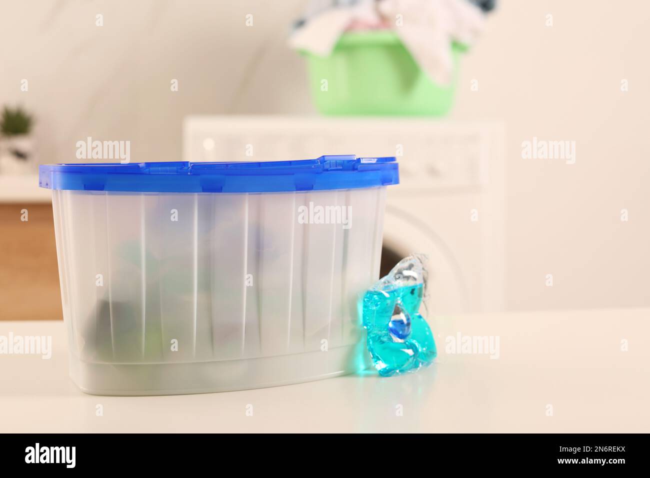 Laundry container and washing detergent capsule on table indoors Stock ...