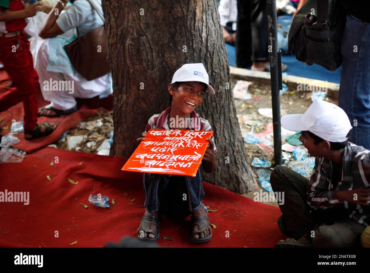 An Indian boy holds a placard and rests against a tree during a protest ...