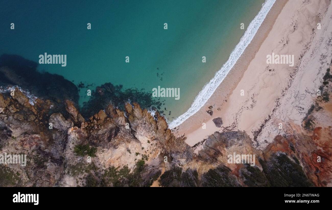Abstract aerial shot of the beach with clear water and rocky shore ...