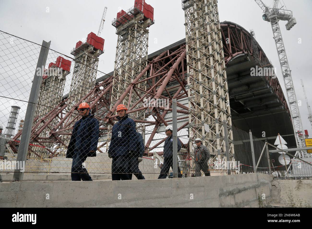 Workers passes by a gigantic steel-arch under construction to cover the ...