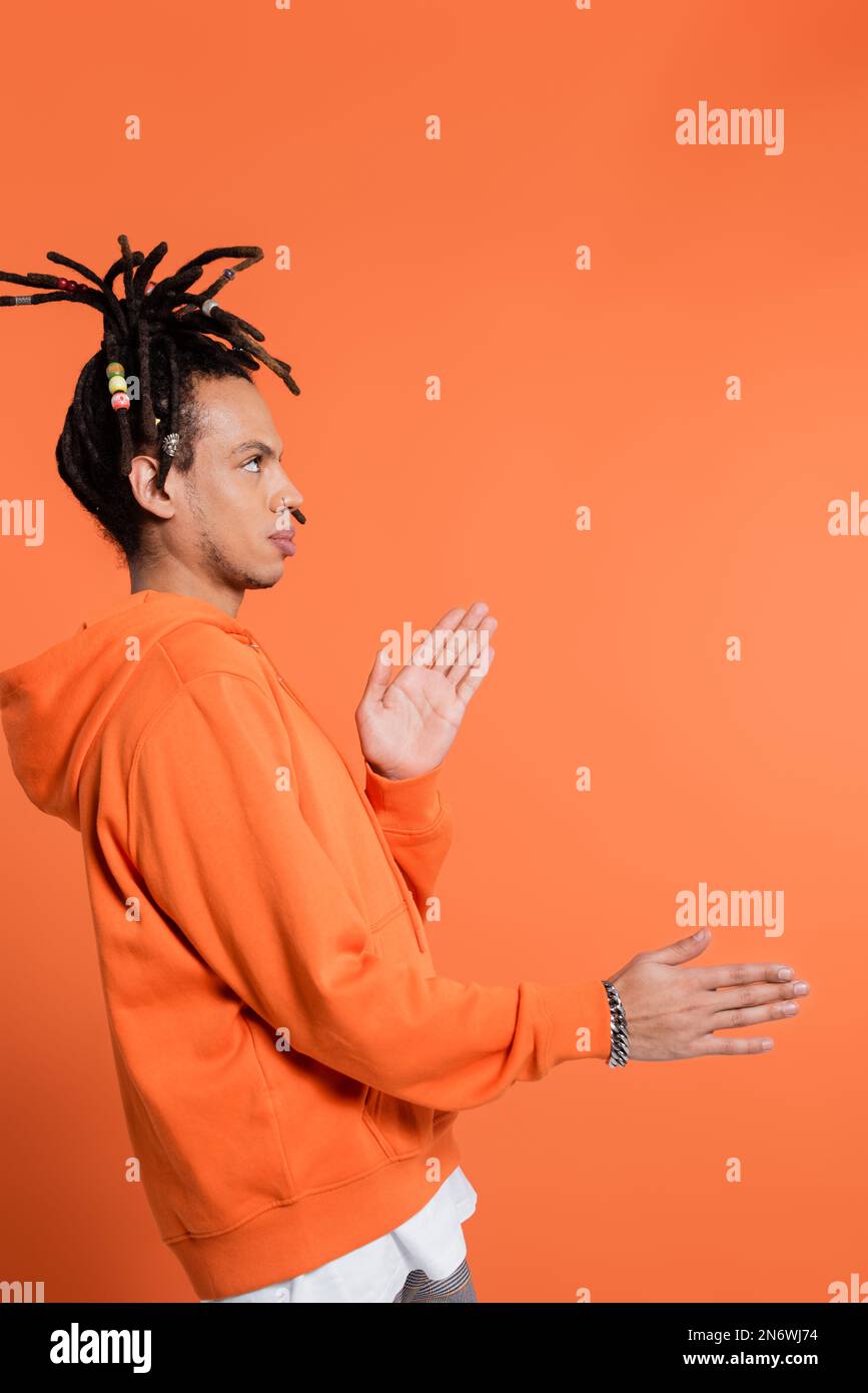side view of multiracial man with dreadlocks looking away and gesturing ...