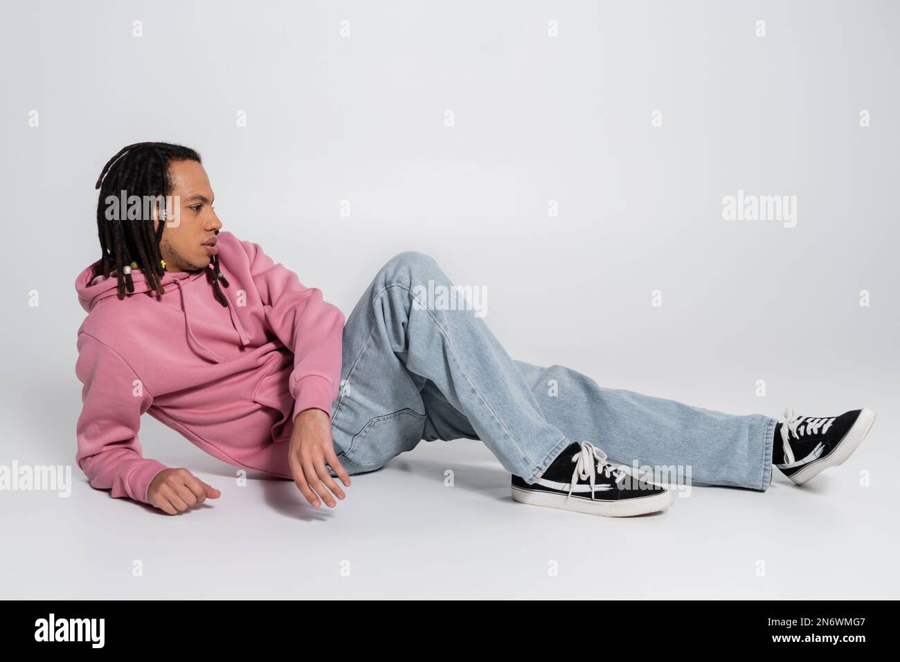 side view of multiracial and pierced man with dreadlocks sitting on ...