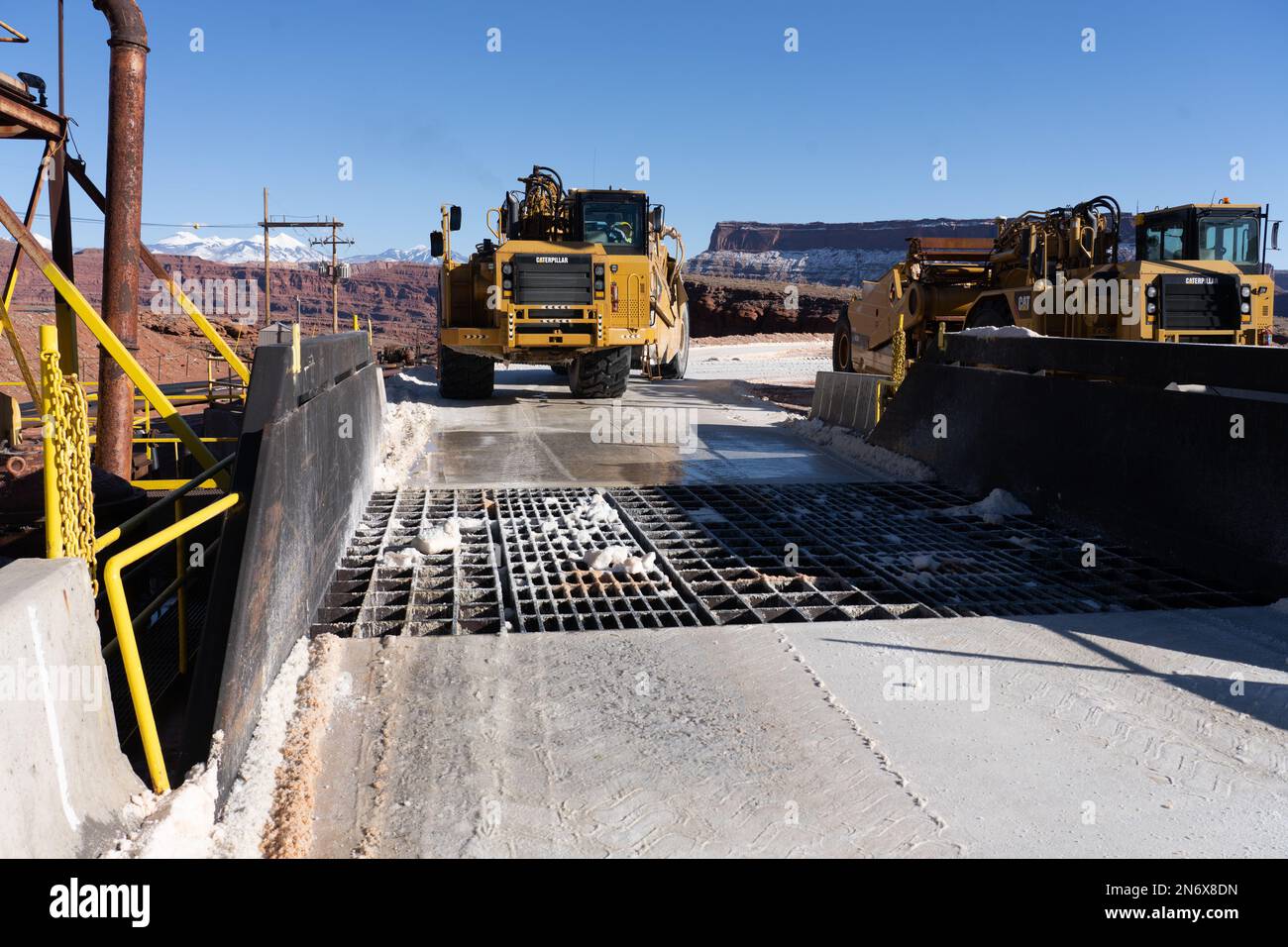 A heavy-duty scraper approaches the grate over a slurry pit to dump a ...