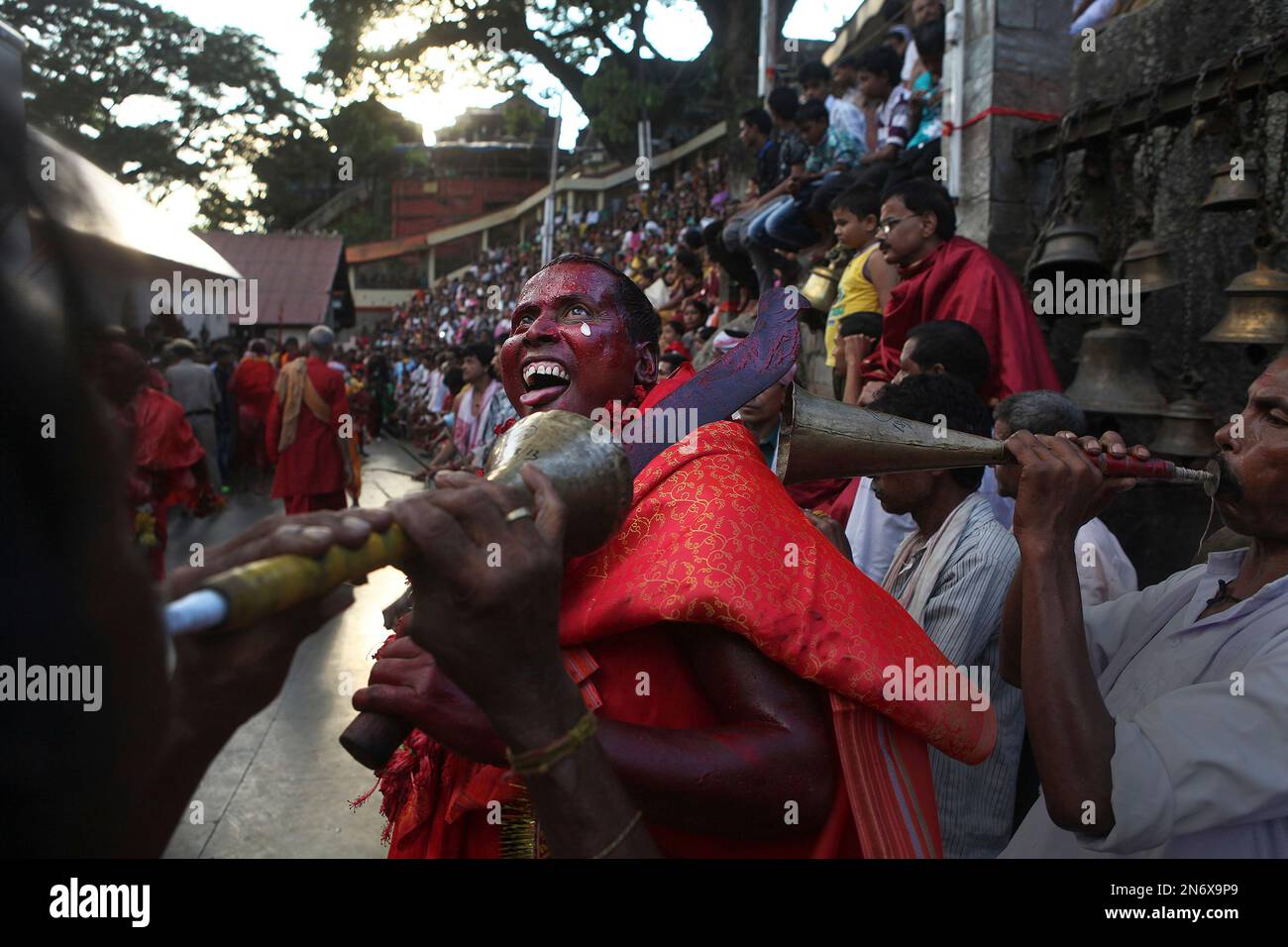 A Hindu priest, face smeared with color and sacrificial blood, gestures ...