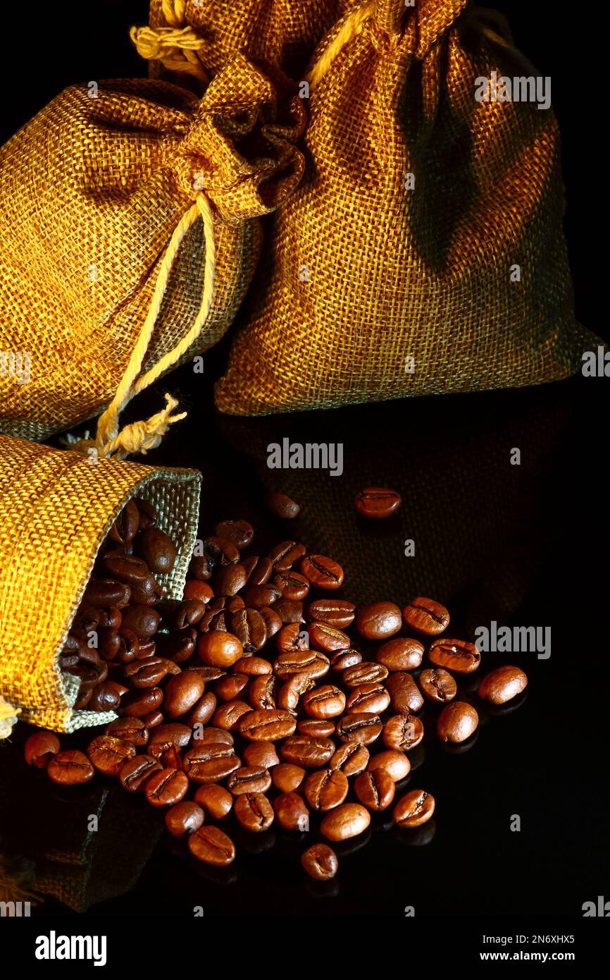 Hessian sacks full of roasted coffee beans spilling out of an open sack on to black glass Stock ...