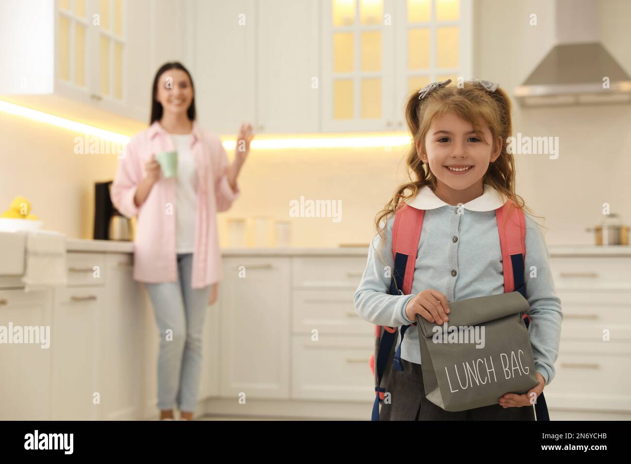 Little girl with lunch bag and mother in kitchen. Getting ready for ...