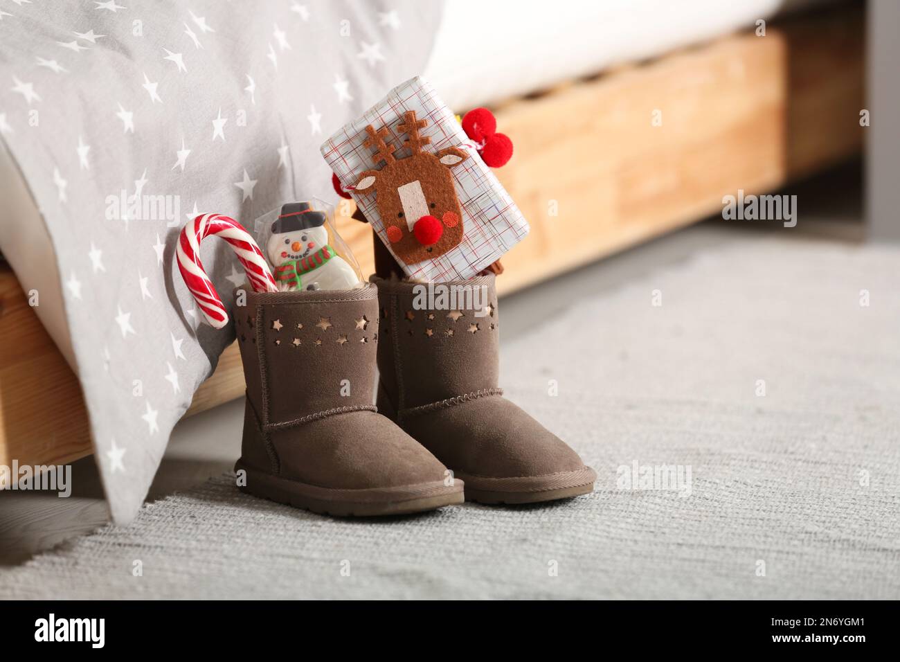 Sweets and gift box in child's boots near bed indoors. St. Nicholas Day ...