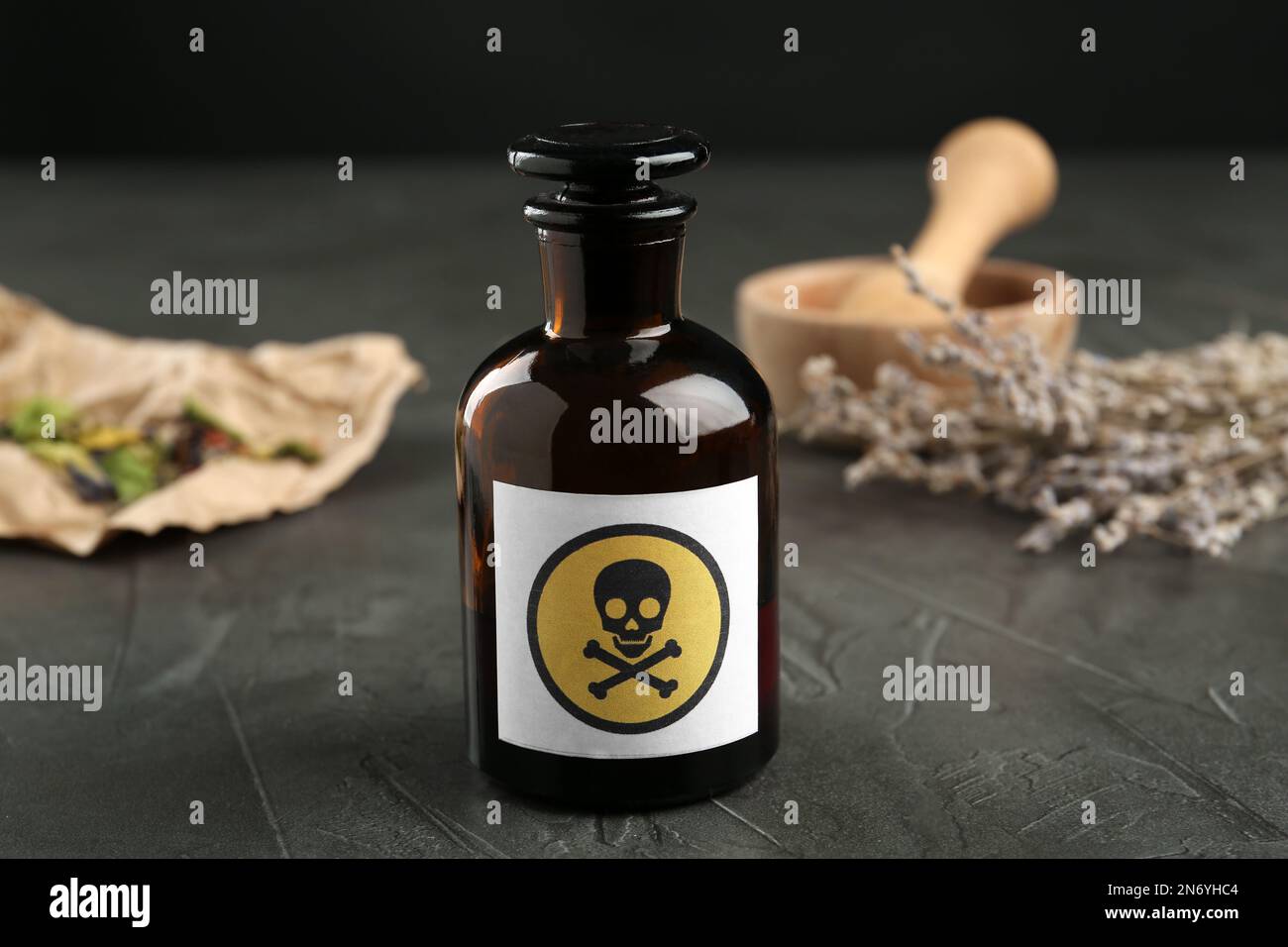 Glass bottle of poison with warning sign and herb on grey stone table ...