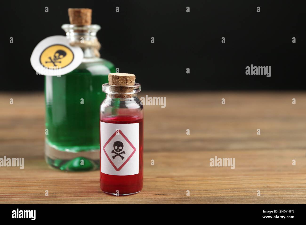 Glass bottle and vial of poison with warning signs on wooden table ...